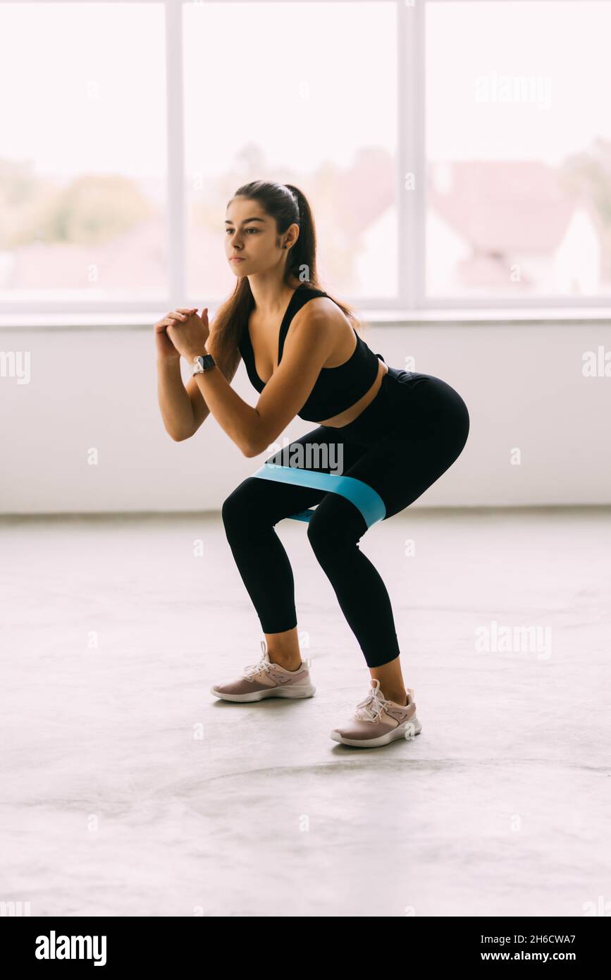 Slim Blonde Woman Doing Squats With Fitness Loop Band Isolated On White