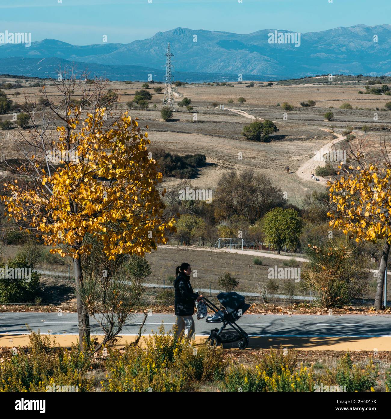 Woman carrying a baby stroller facing west towards El Pardo mountains ...