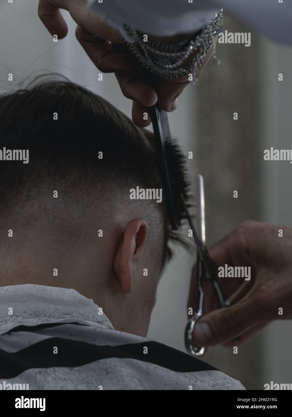 Vertical shot of a barber's hands cutting a client's hair with scissors ...