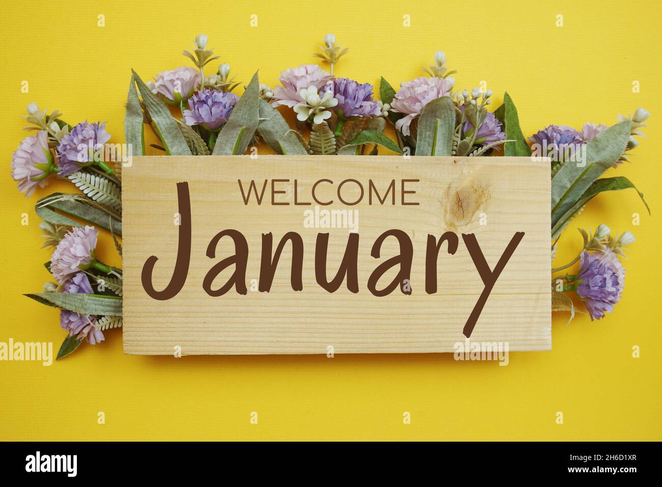 Welcome January text on wooden board with flowers frame on yellow ...