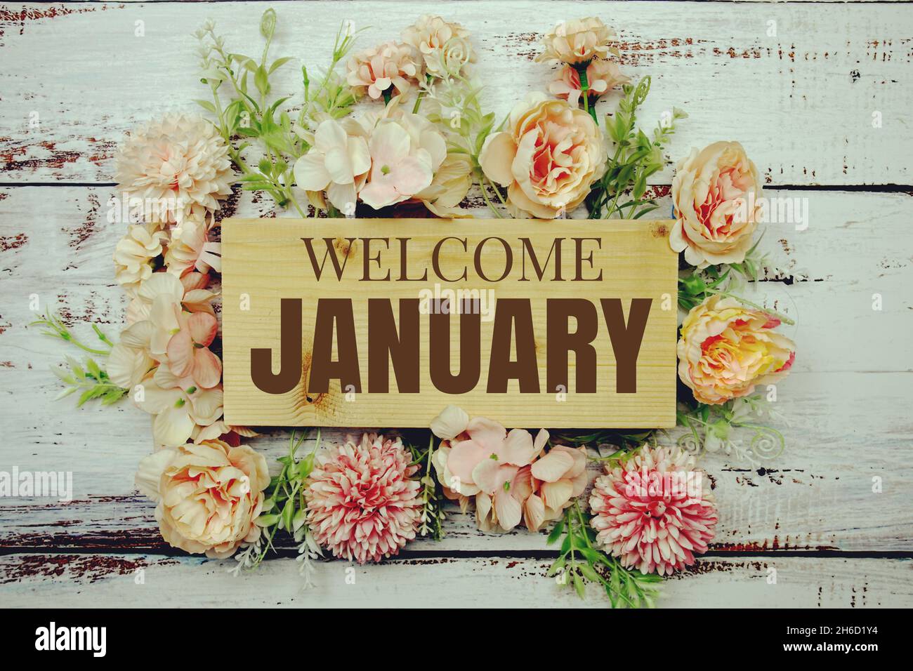 Welcome January text on wooden board with flowers frame on wooden ...
