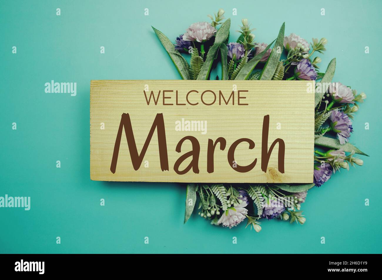 Welcome March text on wooden board with flowers frame on blue ...