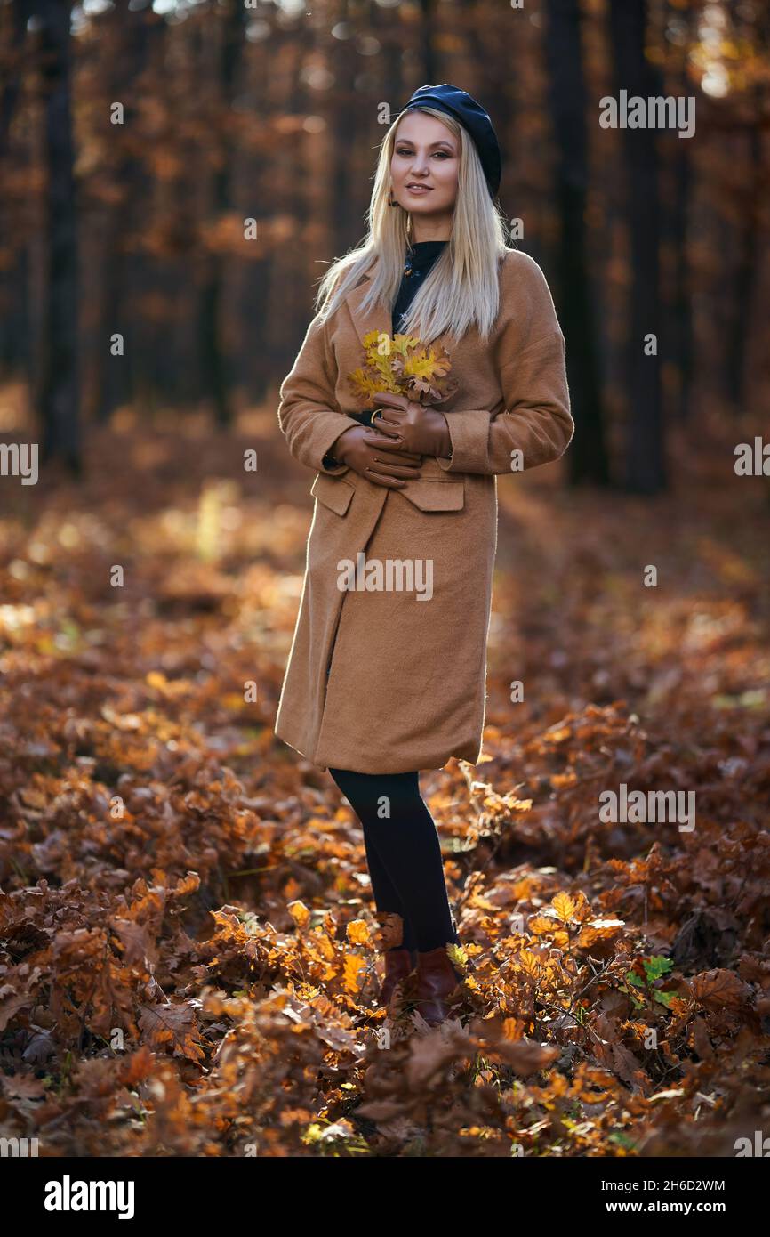 Autumnal candid portrait of a blonde young woman in coat and cap in the ...