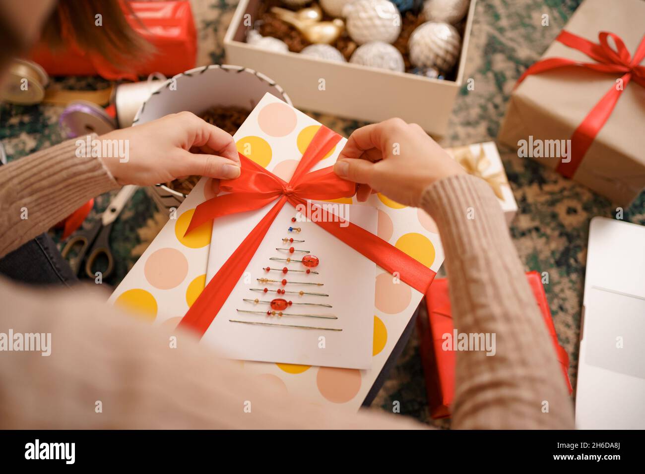 Close up female hands tying a red ribbon bow on a craft gift box. Woman ...