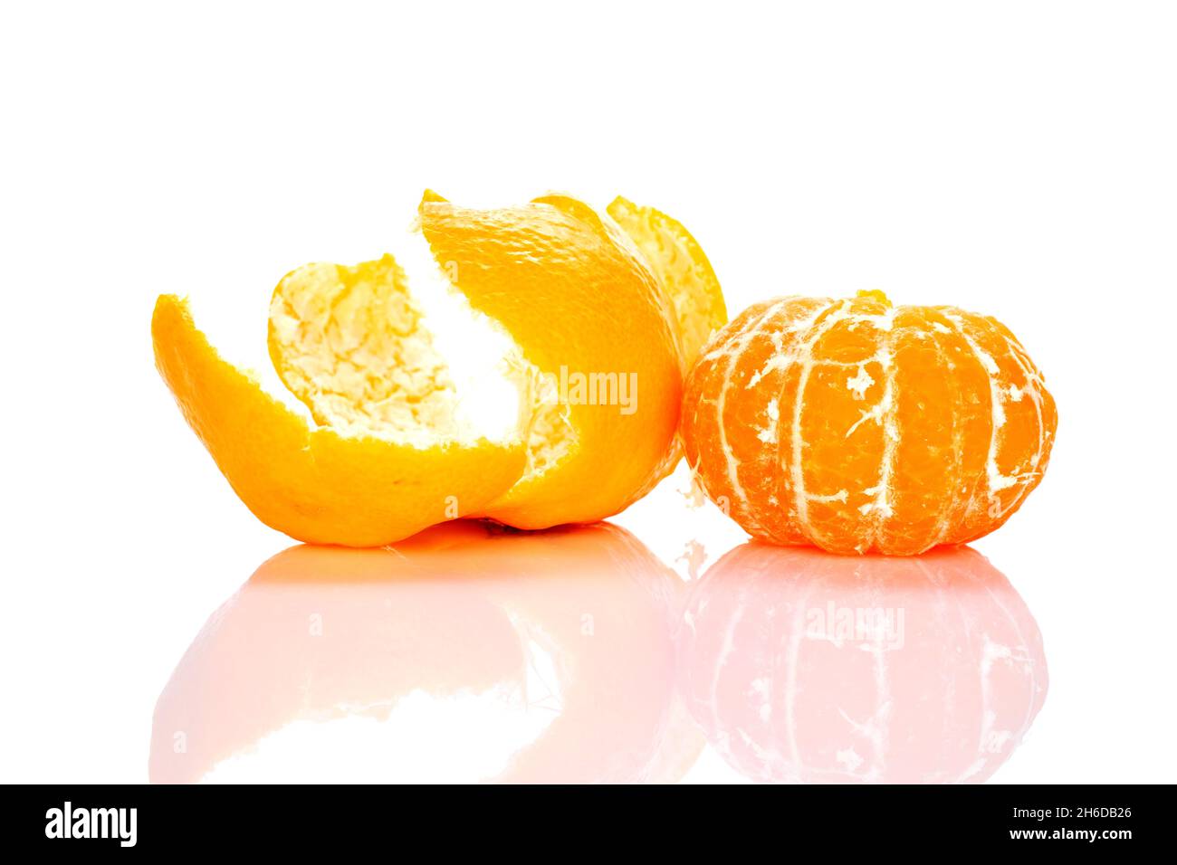 One whole peeled bright yellow tasty mandarin. Nearby is the skin of ...