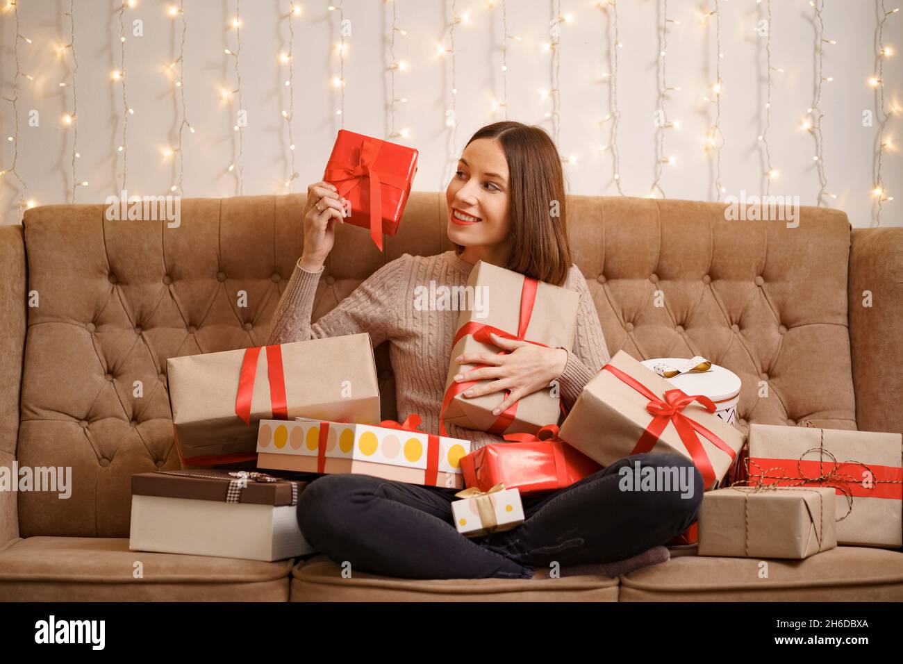 Happy young woman hugging many present boxes sitting crossed legs on a ...