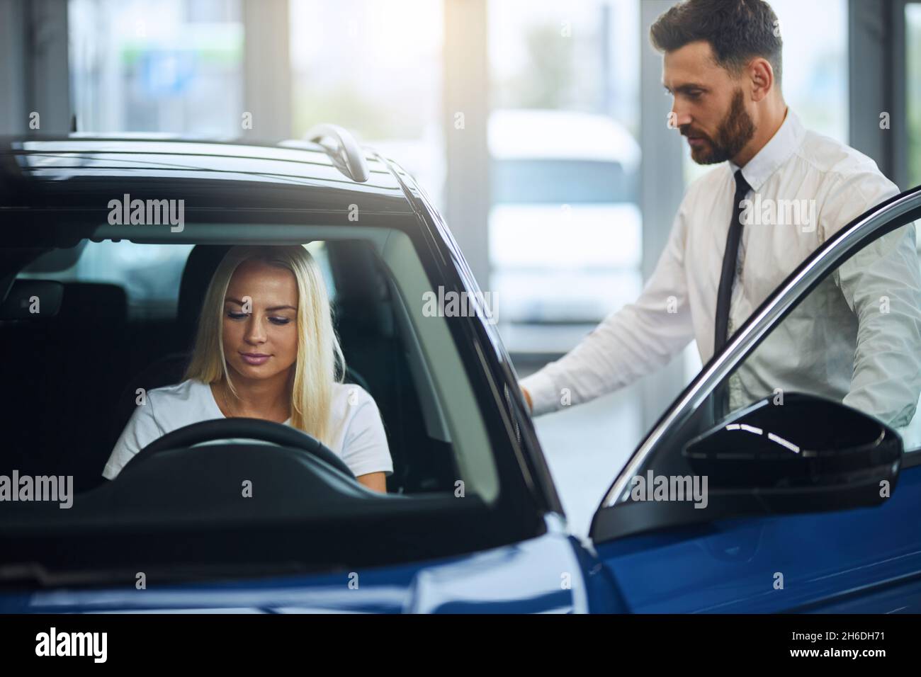 Professional car dealer presenting female buyer luxury modern car at ...