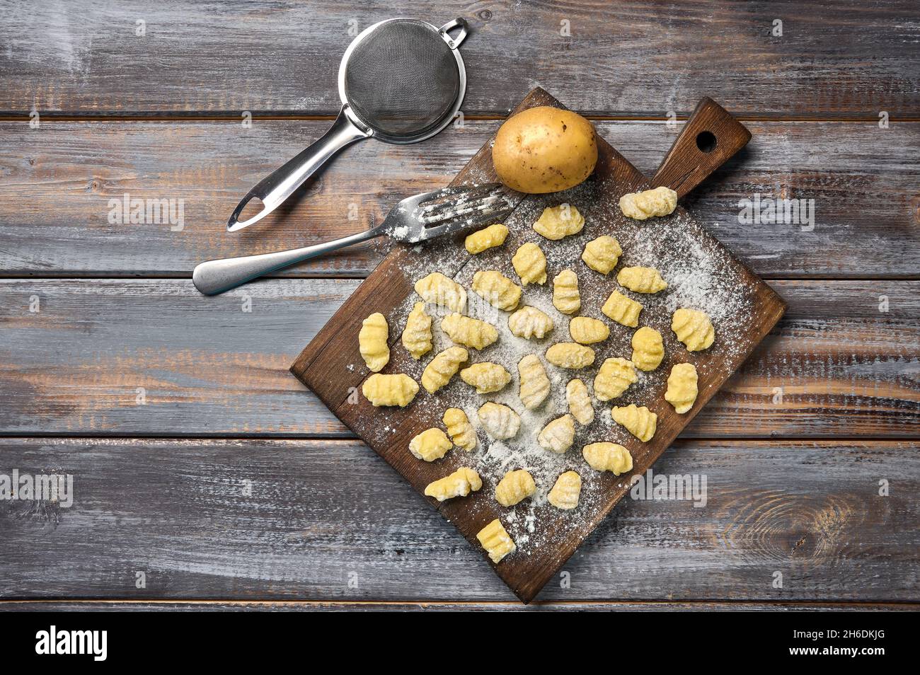 Top view raw uncooked potato gnocchi, sieve and fork on wooden cutting ...