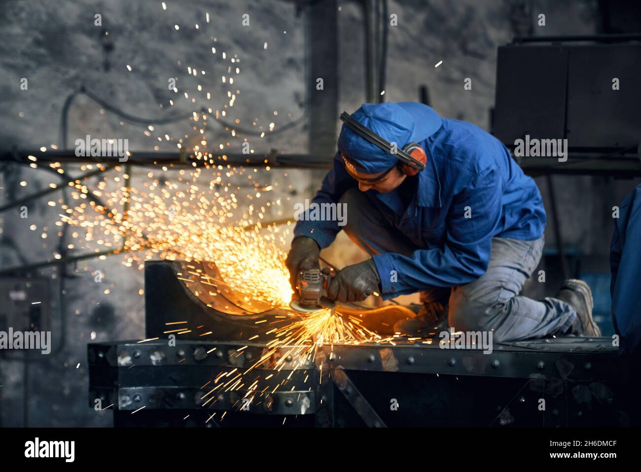 Industrial worker in special protective clothes polishing metal ...