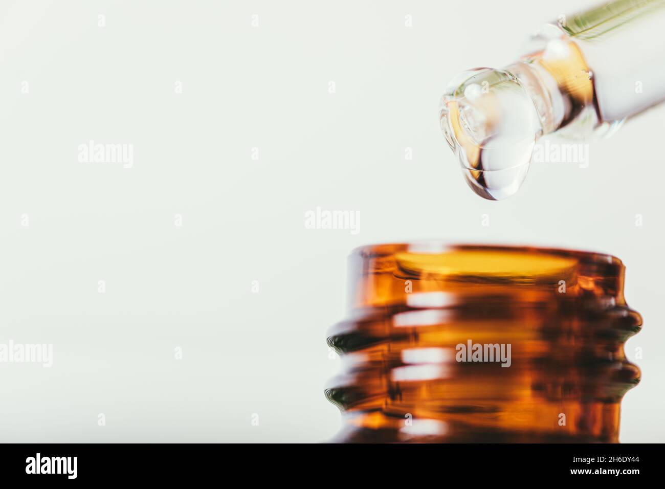 Essential oil drop from pipette into bottle on white background, close ...