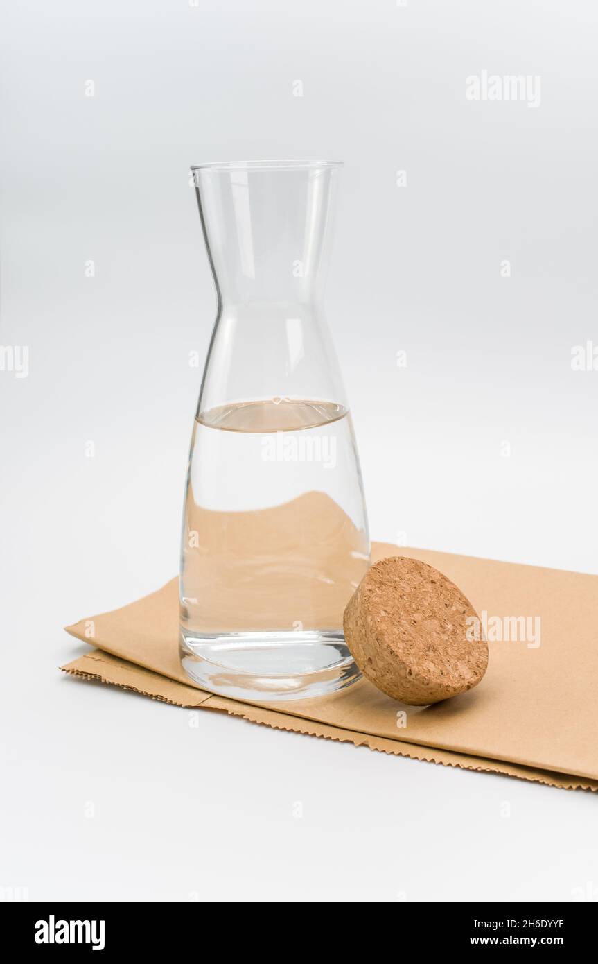 glass carafe with fresh water and cork lid on a white and brown paper ...