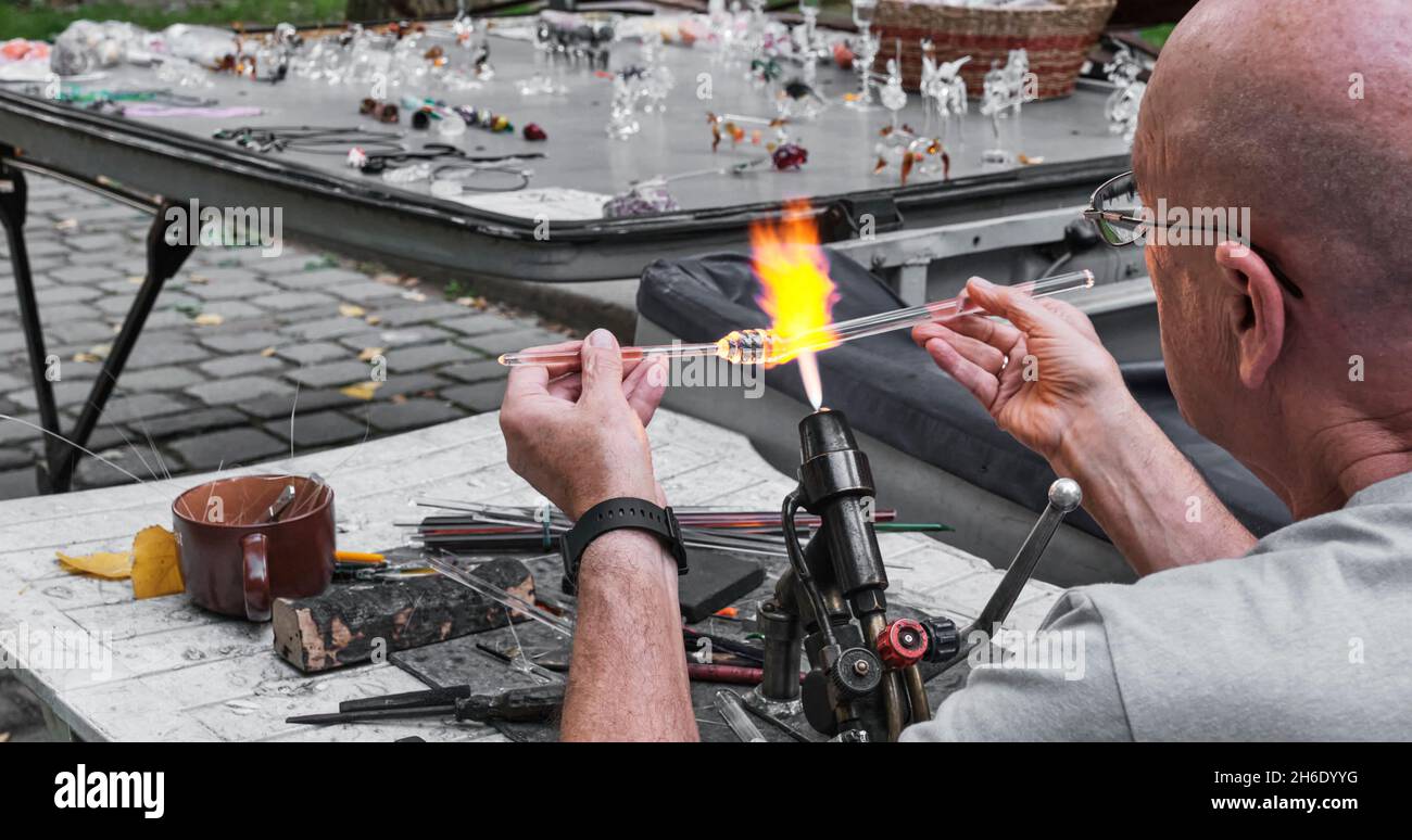 Senior man glassblower holding glass rod over burner flame. Process of ...