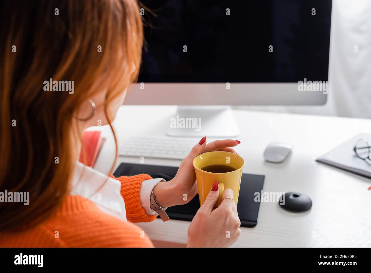 retoucher holding cup of tea near blurred graphic tablet and monitor ...