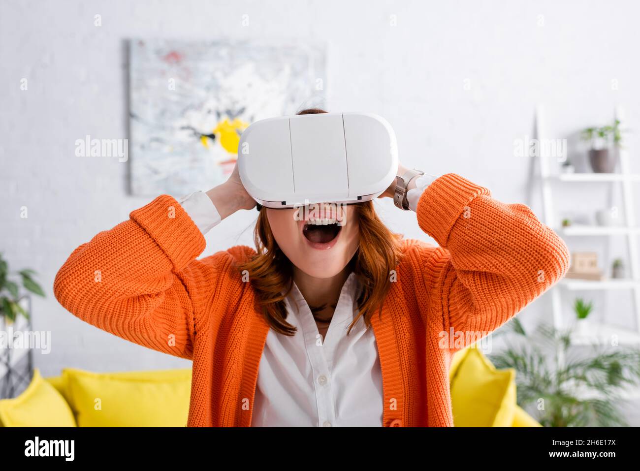 shocked woman screaming and touching head while gaming in vr headset ...