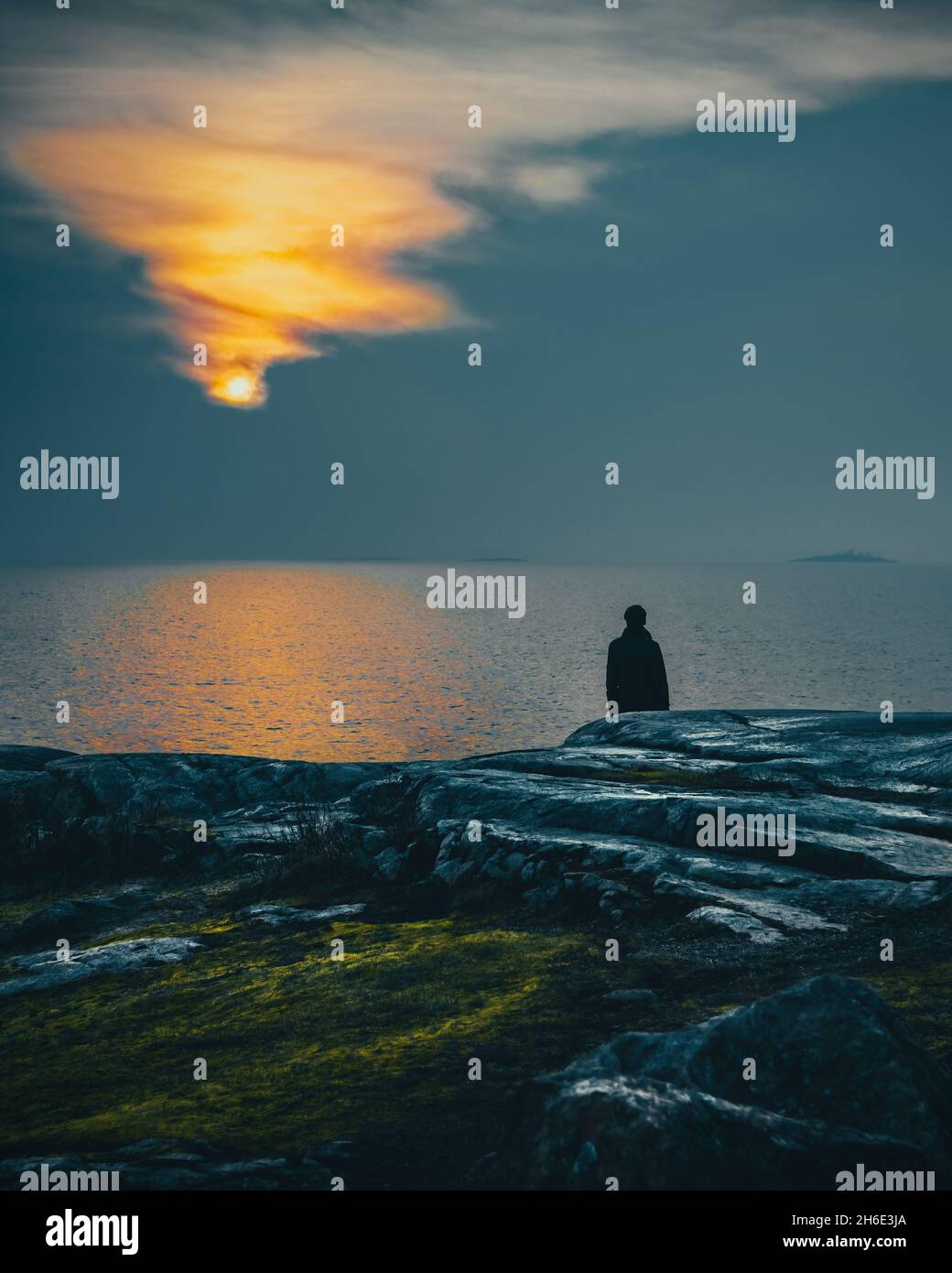 Man standing alone on the rock, watching sunset over sea, enjoying ...