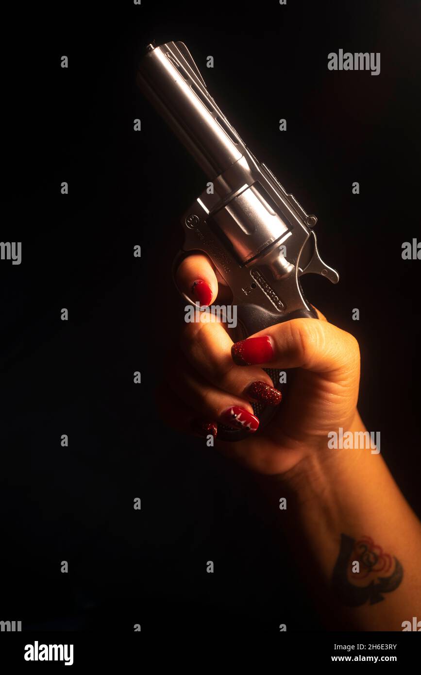 Lady spy detective with painted red nail varnish holding pistol gun at ...