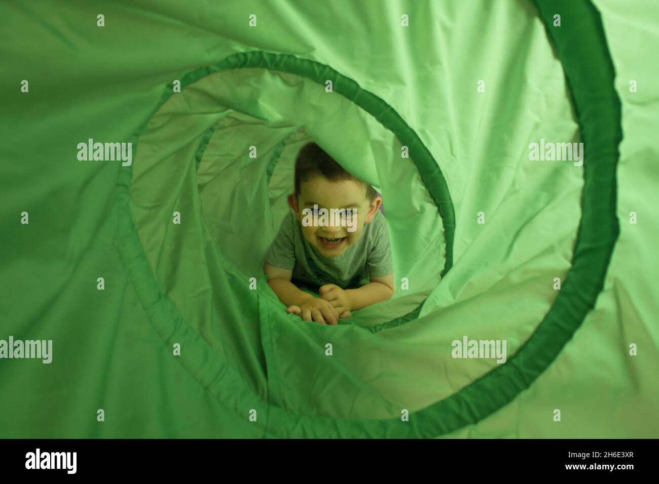 3 year old toddler boy crawling through a kids fabric tunnel in house ...