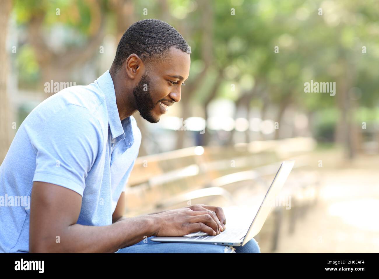 Side view portrait of a happy man with black skin using laptop sitting ...