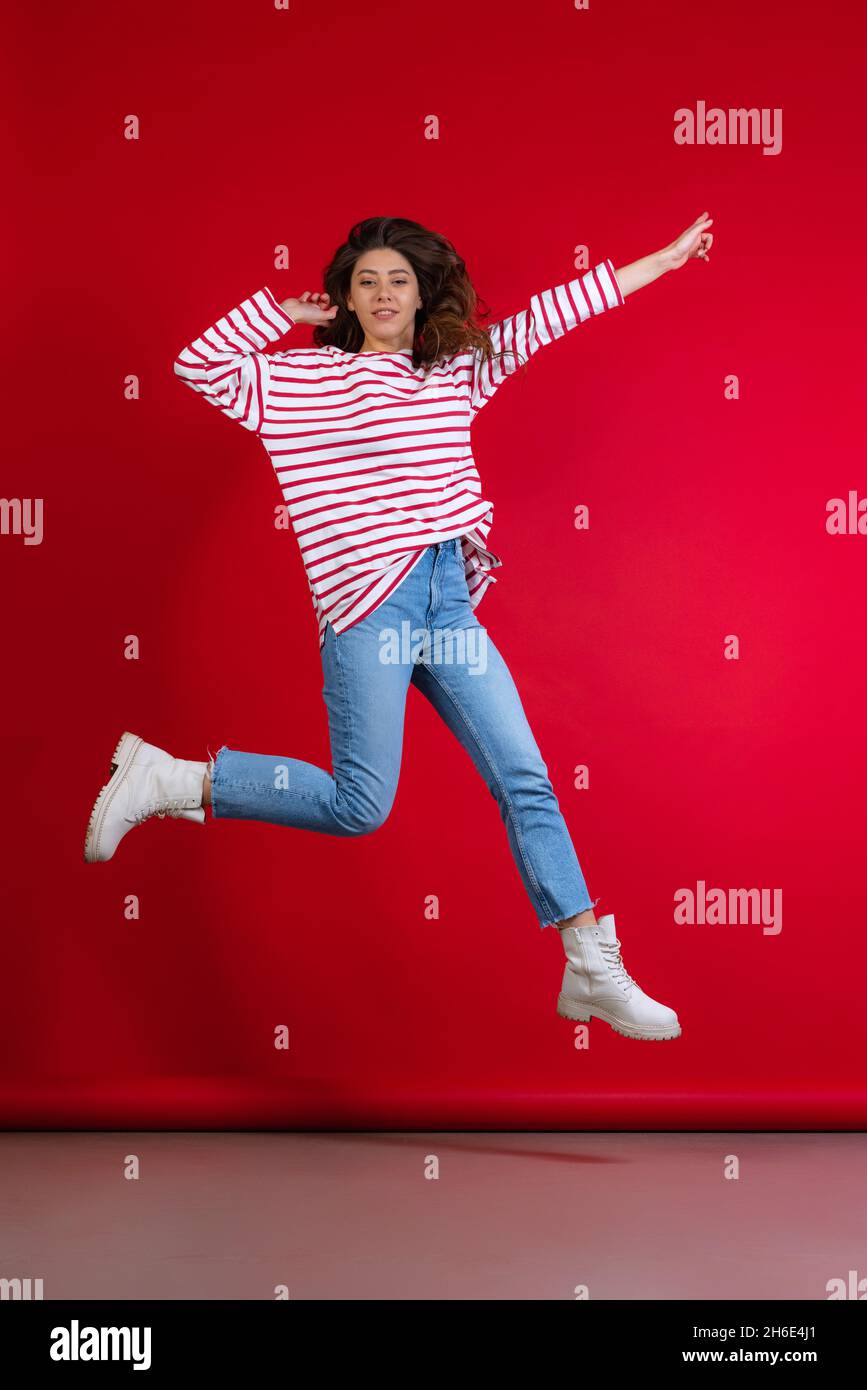 Emotional young beautiful girl in sweater and jeans jumping isolated on ...