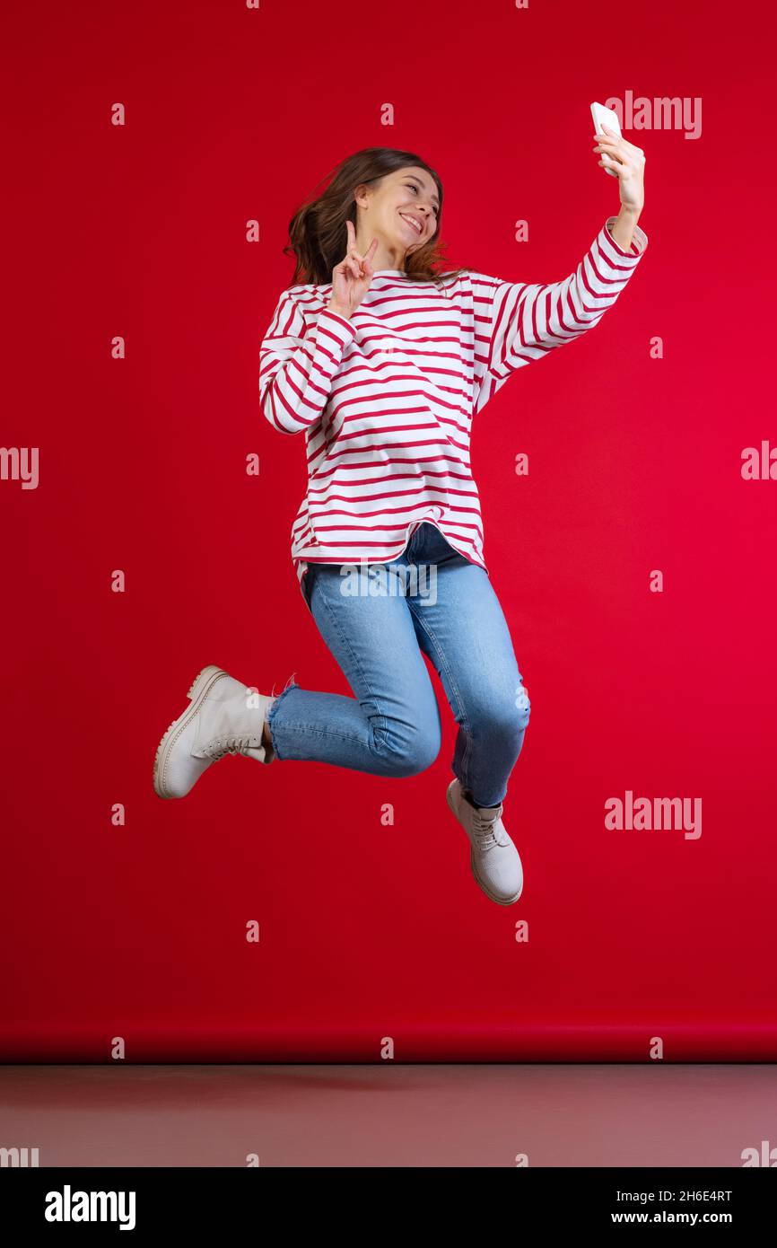 Emotional young beautiful girl in sweater and jeans taking selfie ...