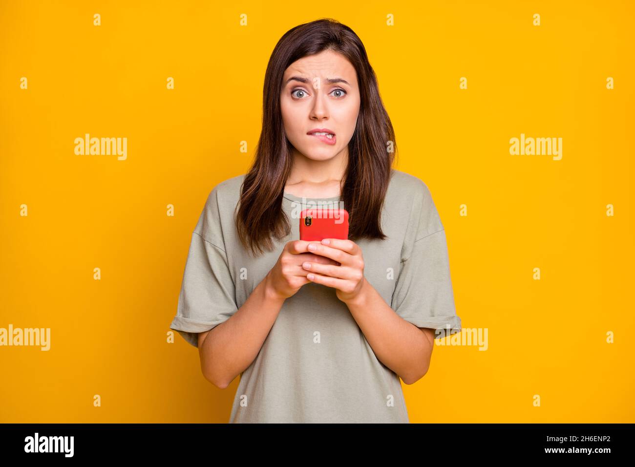 Portrait of pretty worried brown-haired girl using gadget biting lip ...
