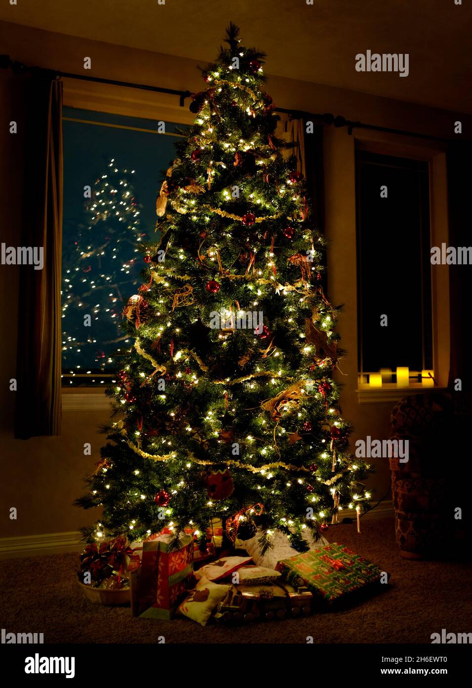 Christmas tree with lights and presents inside a home with big windows ...