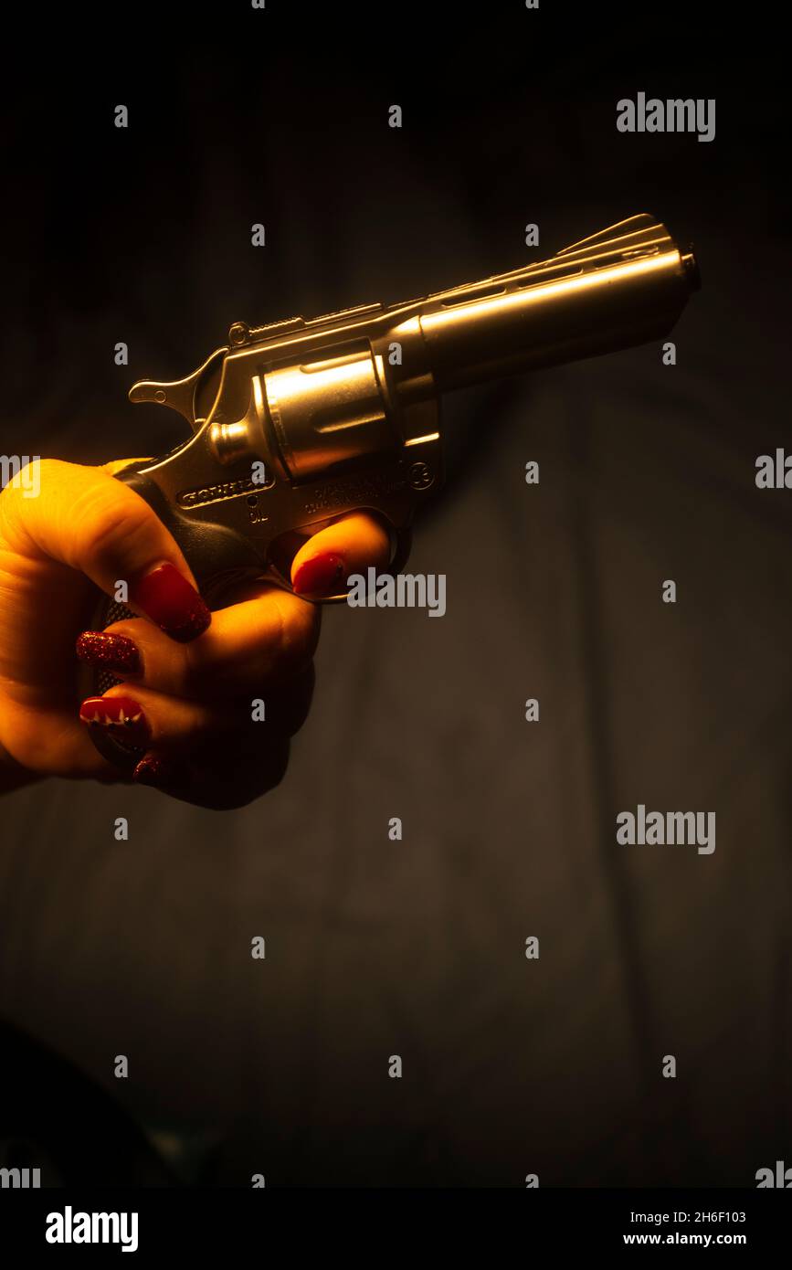 Lady spy detective with painted red nail varnish holding pistol gun at ...
