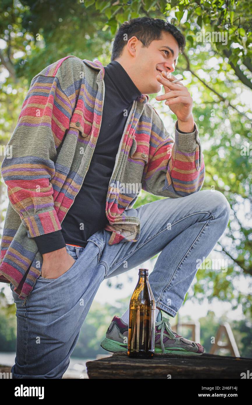 Moody man enjoys life and drinks beer from bottle. Wooden bench with ...