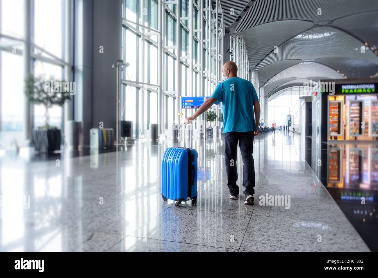 Man pulling suitcase in modern airport terminal. Travelling guy wearing ...