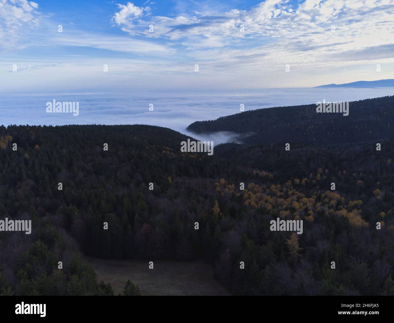 aerial view of a hill plateau with fog creeping up from the valley ...