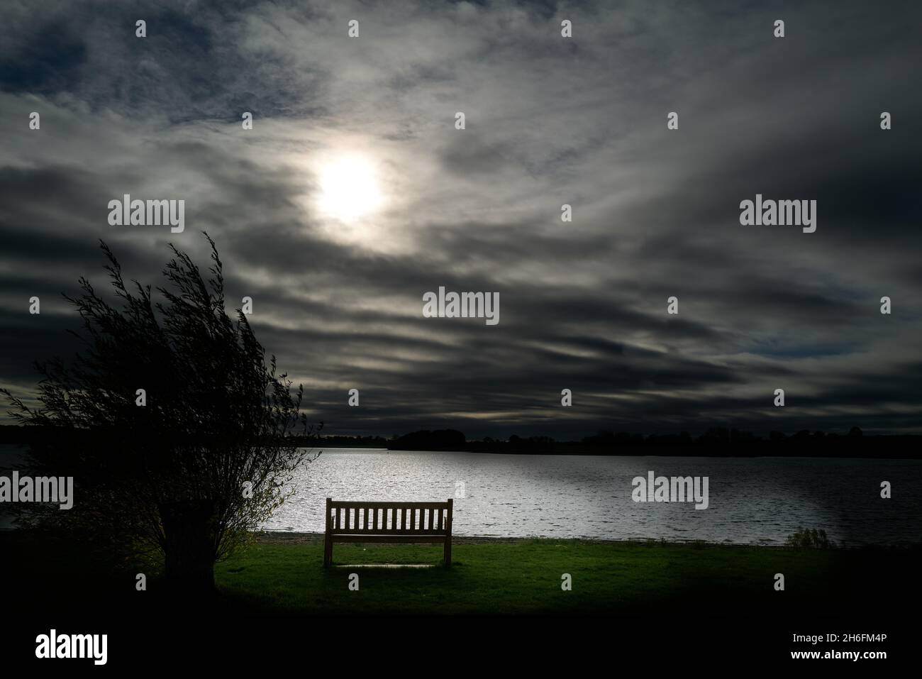 Unoccupied lone bench overlooking a lake under dark cloud Stock Photo ...