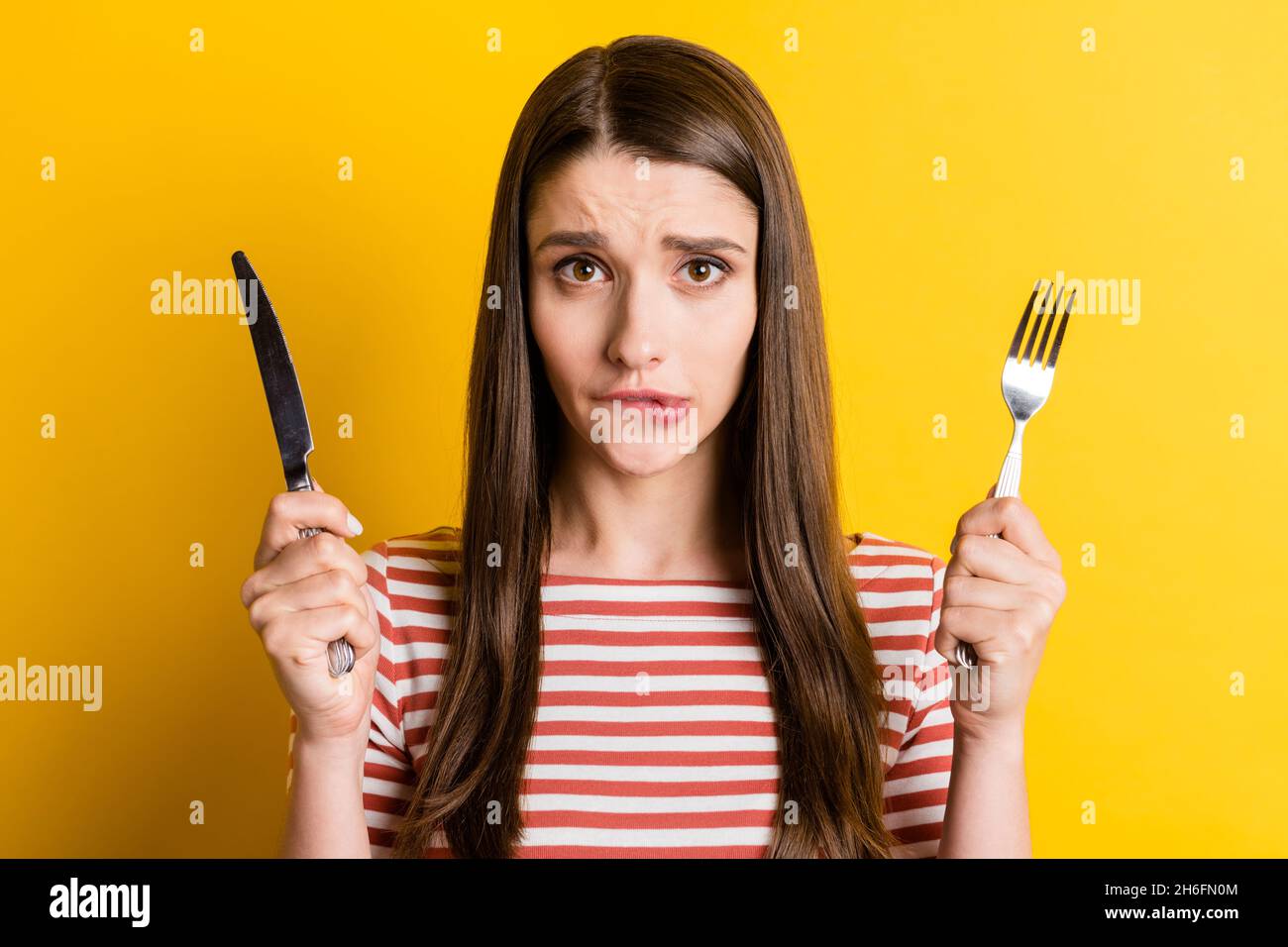 Portrait of attractive girlish hungry girl holding cutlery biting lip ...