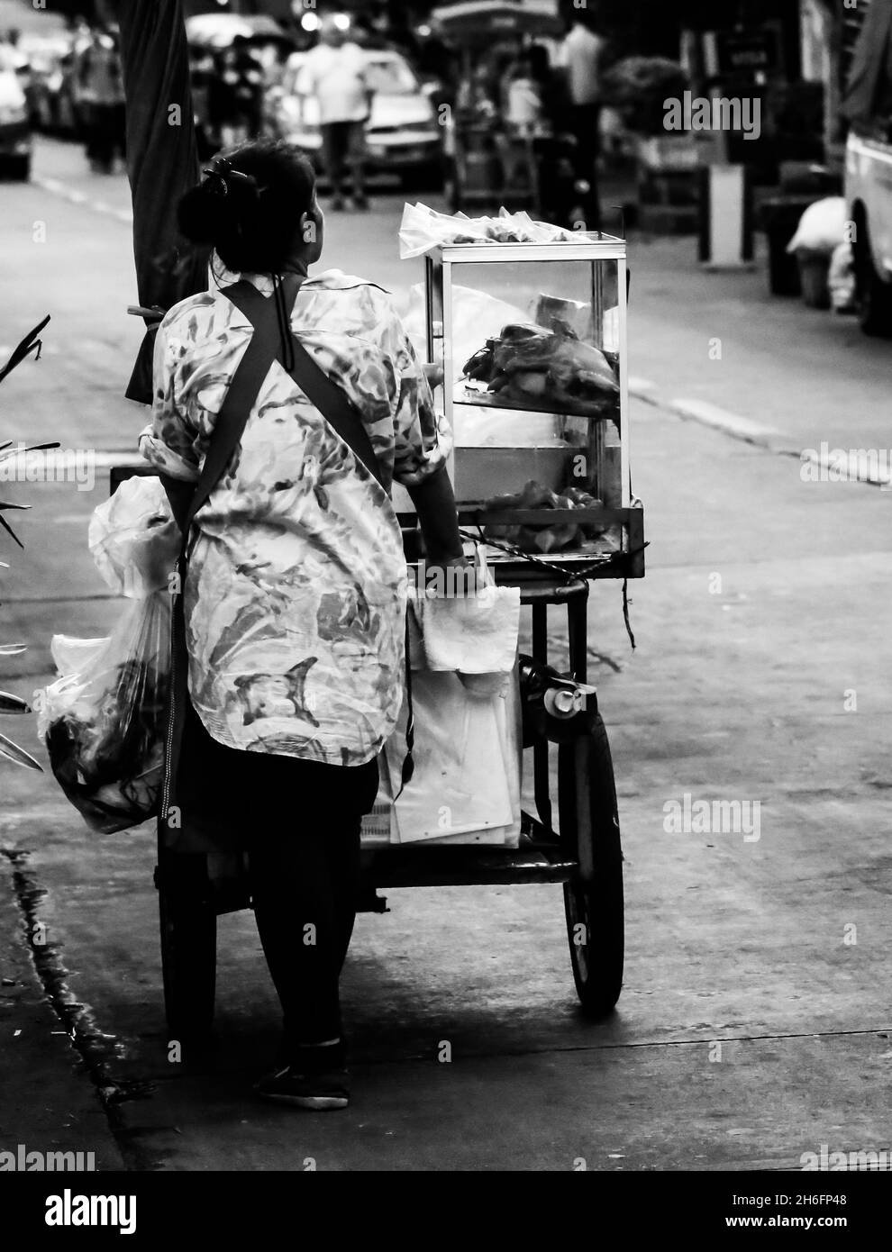 Vertical shot of a lady selling something on a street in grayscale ...