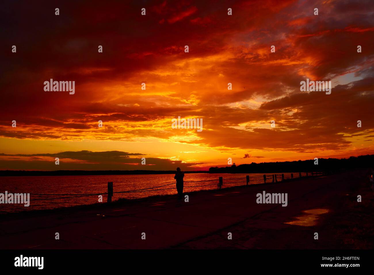 Sad boy on the bridge stands under sky and reflective water surface ...