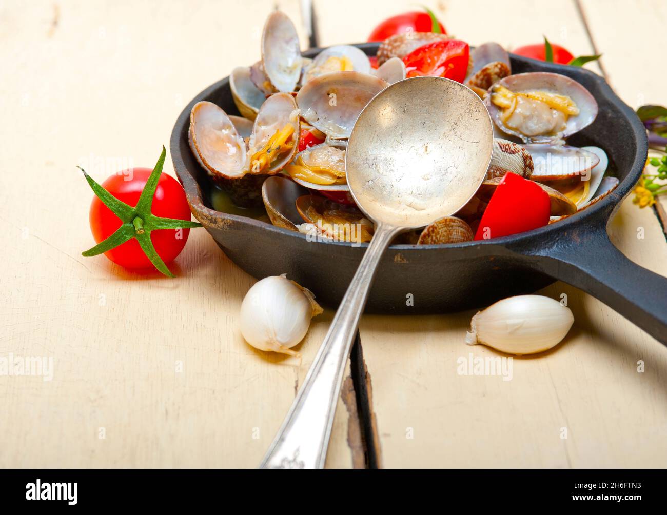 fresh clams stewed on an iron skillet over wite rustic wood table Stock ...
