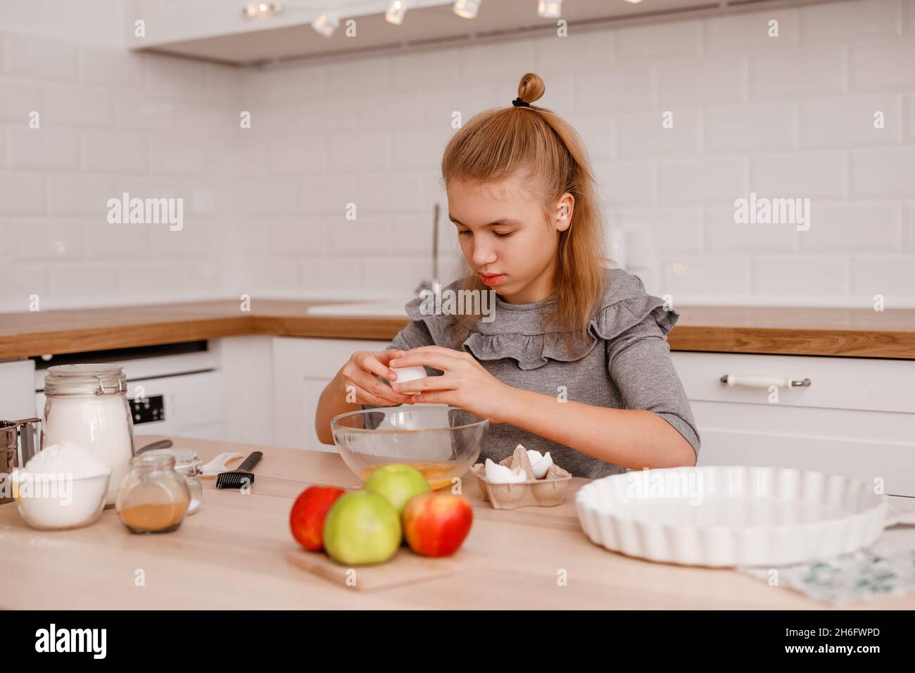 Blonde teenage girl in a gray dress is going to cook traditional apple ...