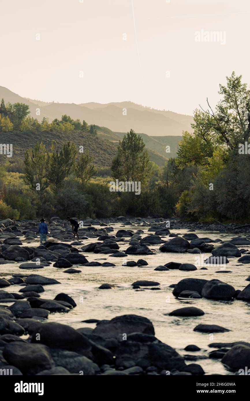 Vertical shot of two people passing the river by the big pieces of ...
