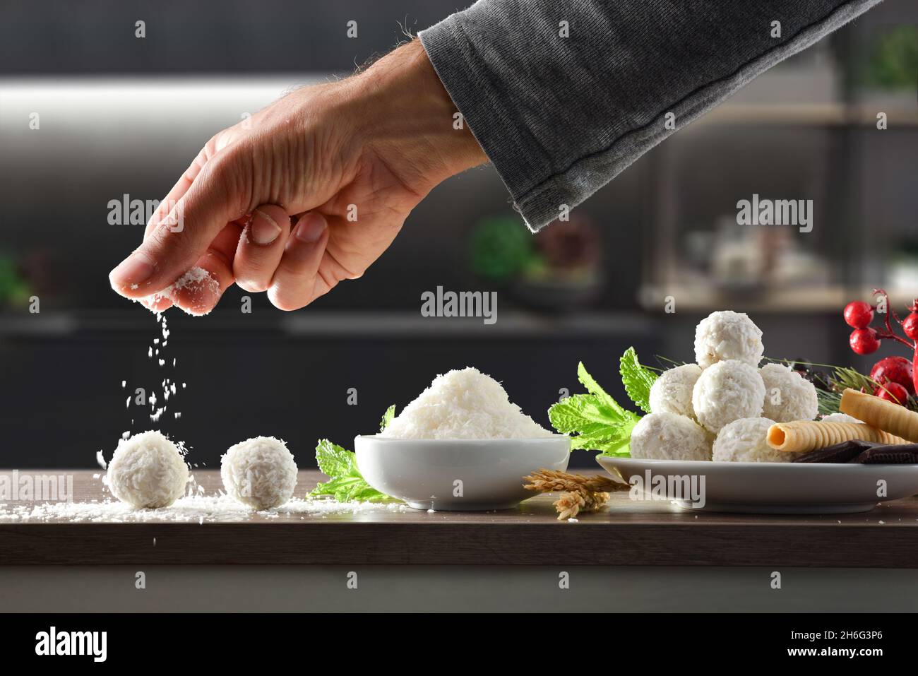 Hand pouring grated coconut over home prepared coconut balls on kitchen ...