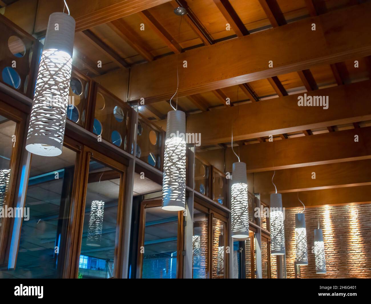 Modern tubular lamps hanging from a wooden ceiling in a big lounge ...