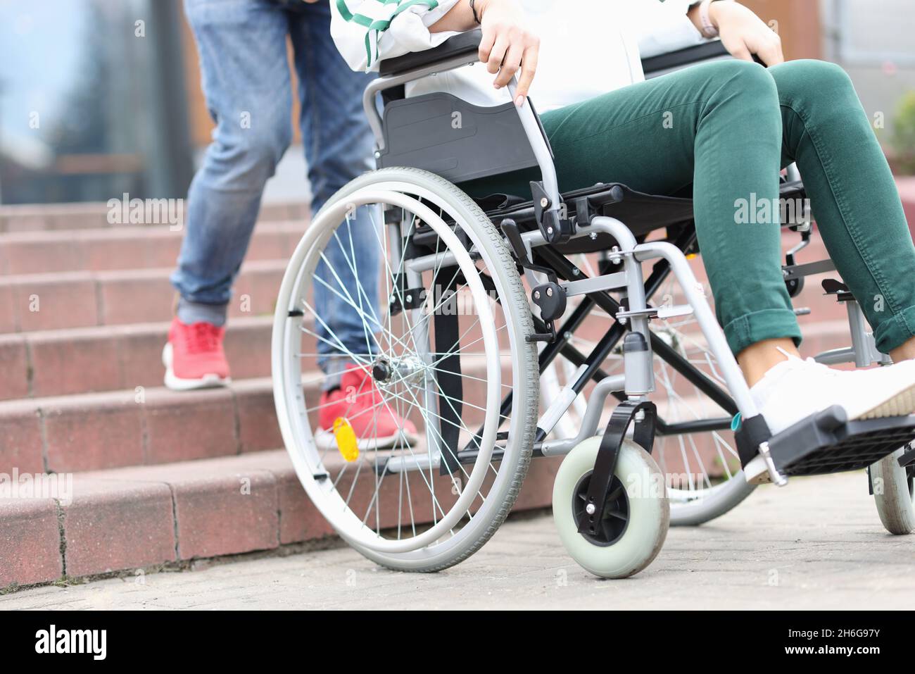 Man lifts wheelchair with a woman on stairs closeup Stock Photo - Alamy