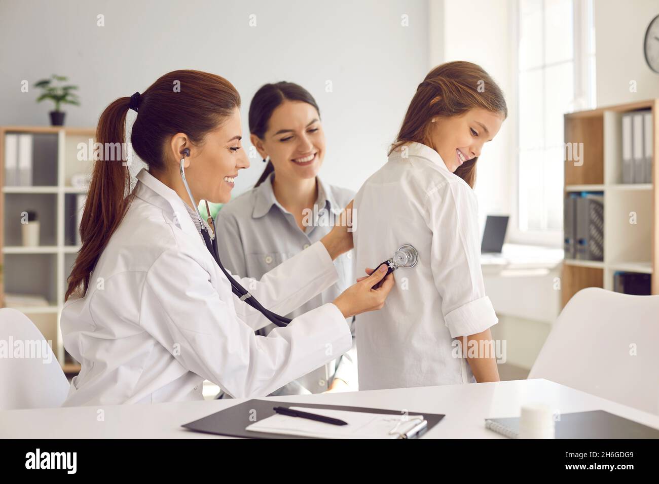 Female doctor puts stethoscope on girl's back and listens to heartbeat ...