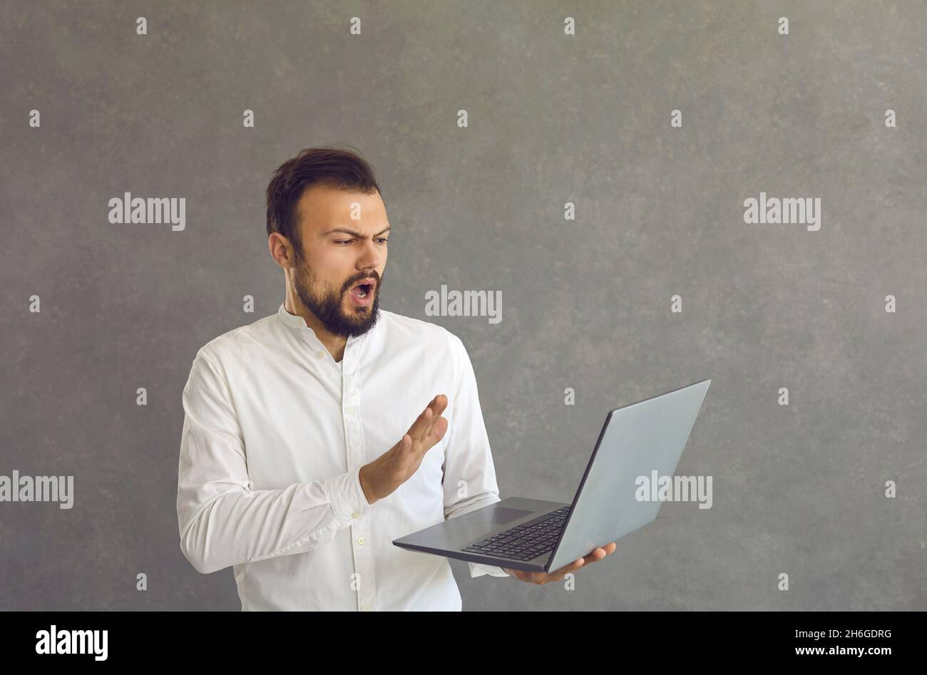 Outraged puzzled Caucasian man looks at laptop screen and makes gesture ...