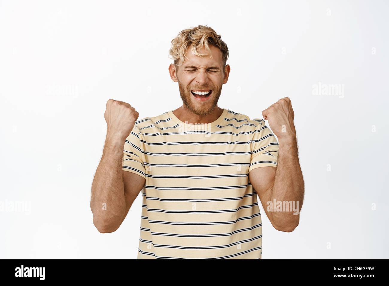 Portrait of enthusiastic blond guy winning, triumphing and making fist ...