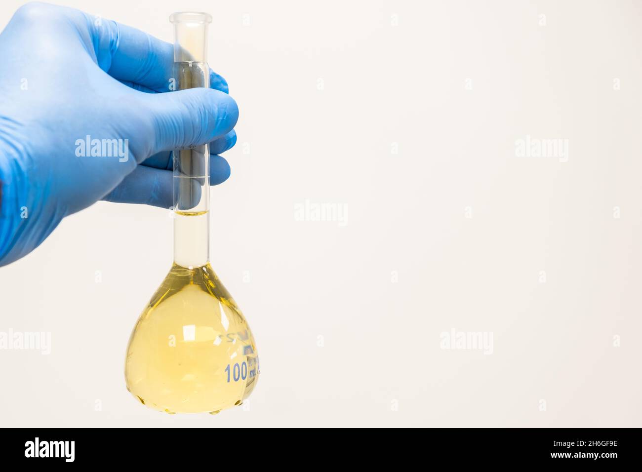 Scientist in blue rubber holding a yellow solution in the flask on the ...