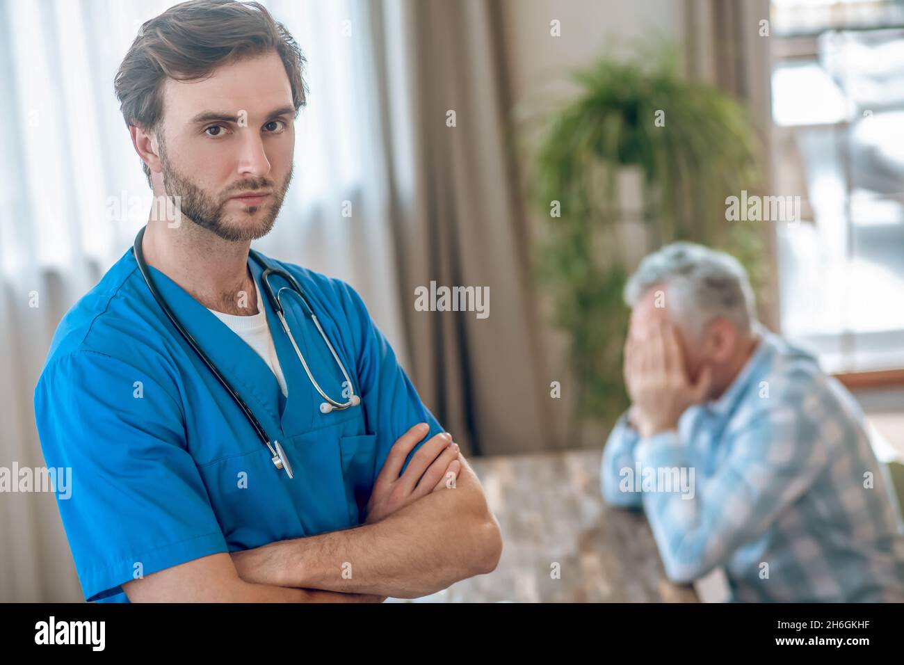Calm young cute doctor standing by his ill patient Stock Photo - Alamy