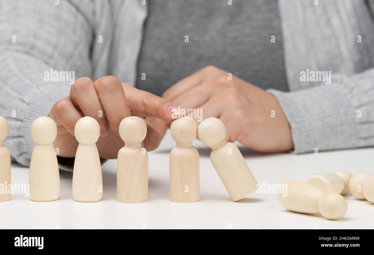 hand stops the fall of wooden figurines of men on a white background ...