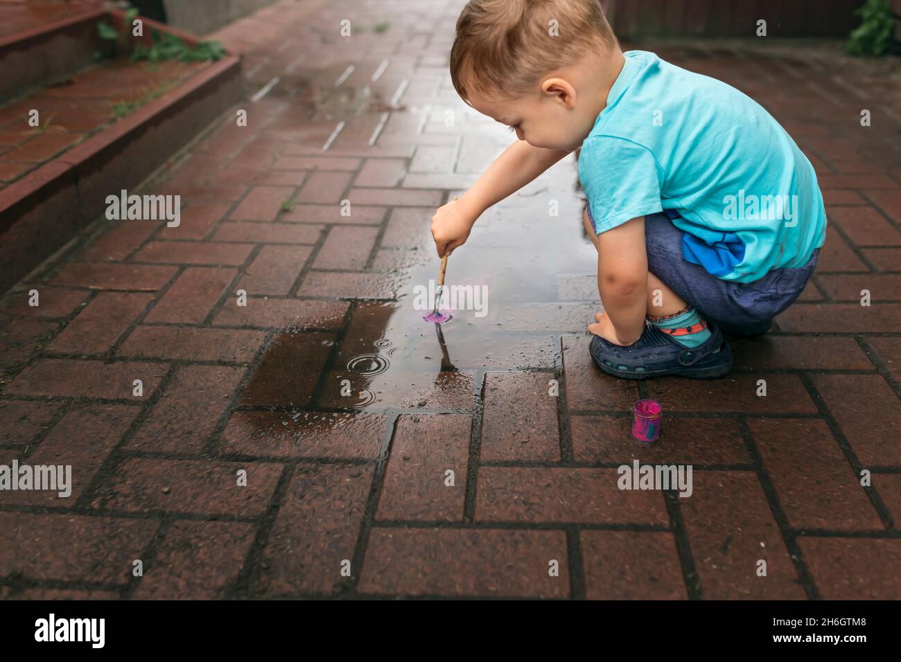Small blonde boy painting pavement with brush and pink paint Stock ...