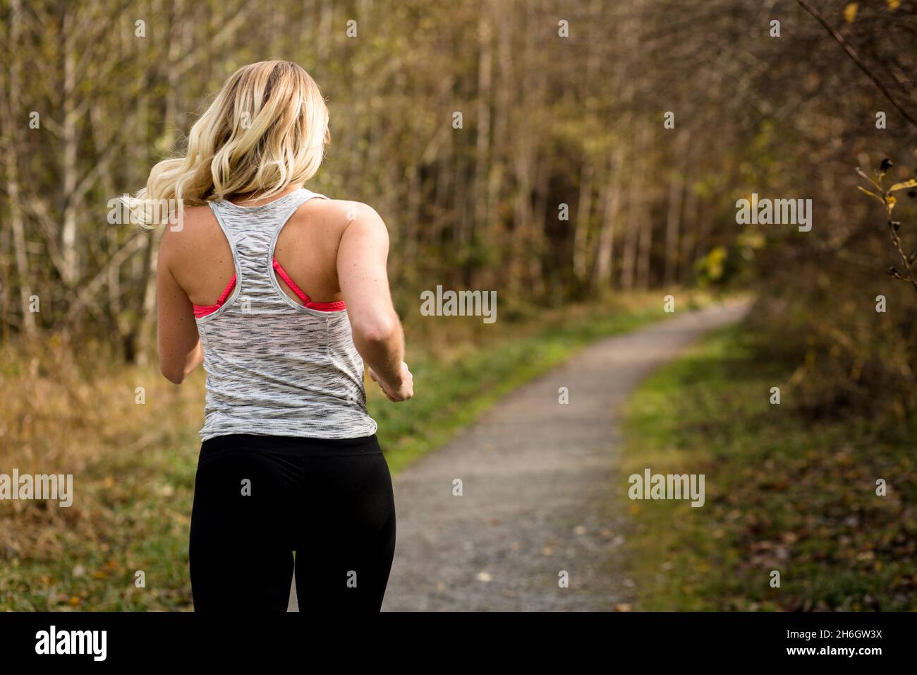 View from behind of blonde woman running on wooded trail Stock Photo ...