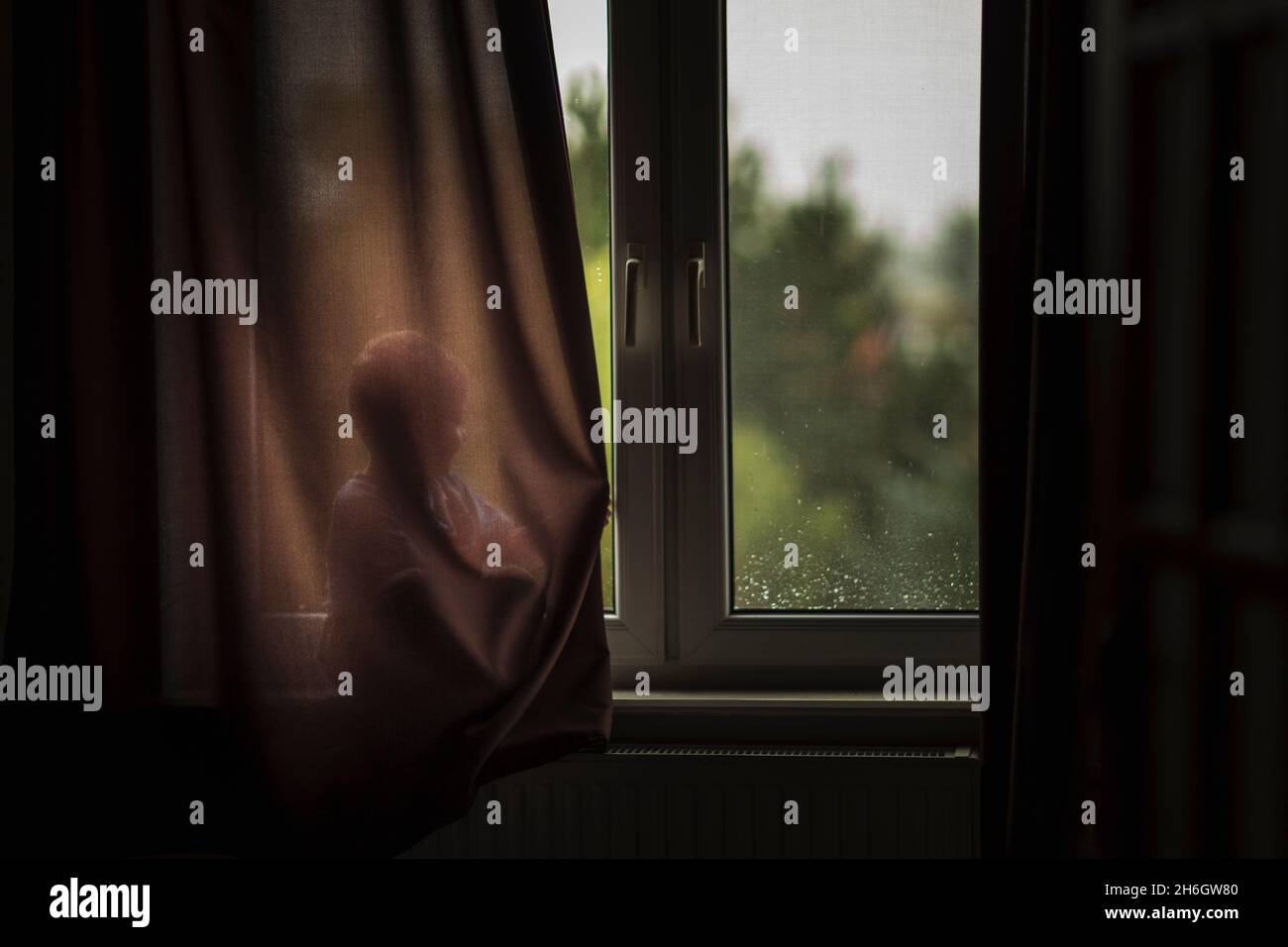 Child sitting on windowsill and hiding behind brown curtain Stock Photo ...