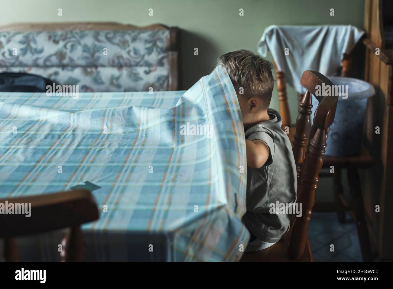 Boy sitting by kitchen table and putting his head under table cl Stock ...